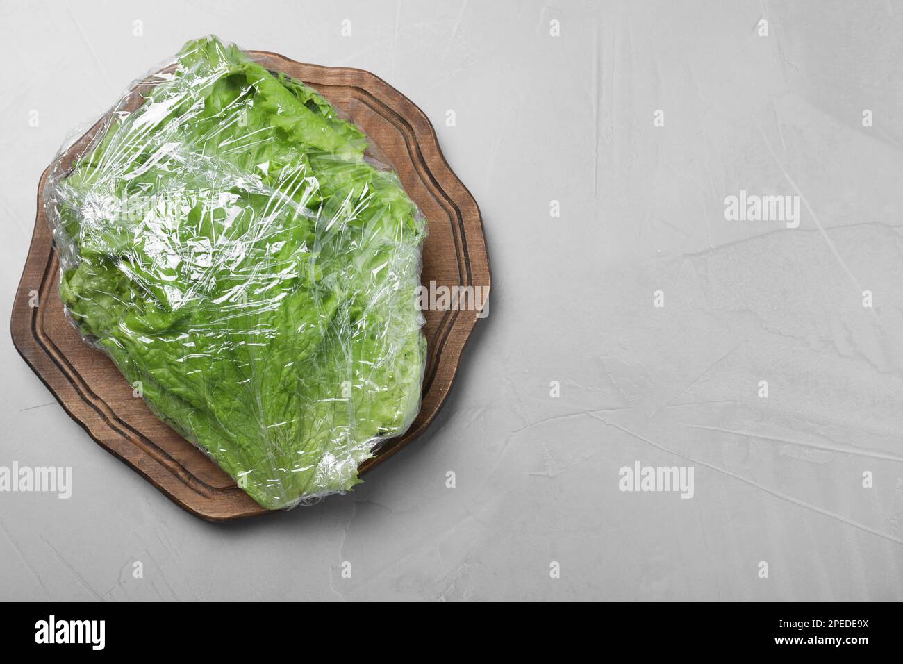 Fresh lettuce in plastic food wrap on light grey table, top view. Space ...