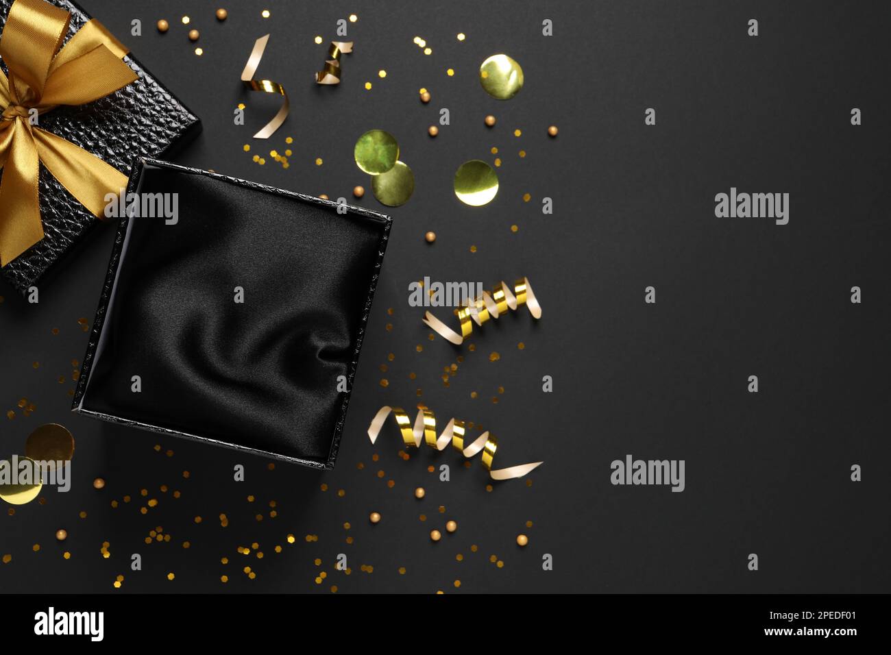 Open gift box, confetti and streamers on black background, flat lay ...
