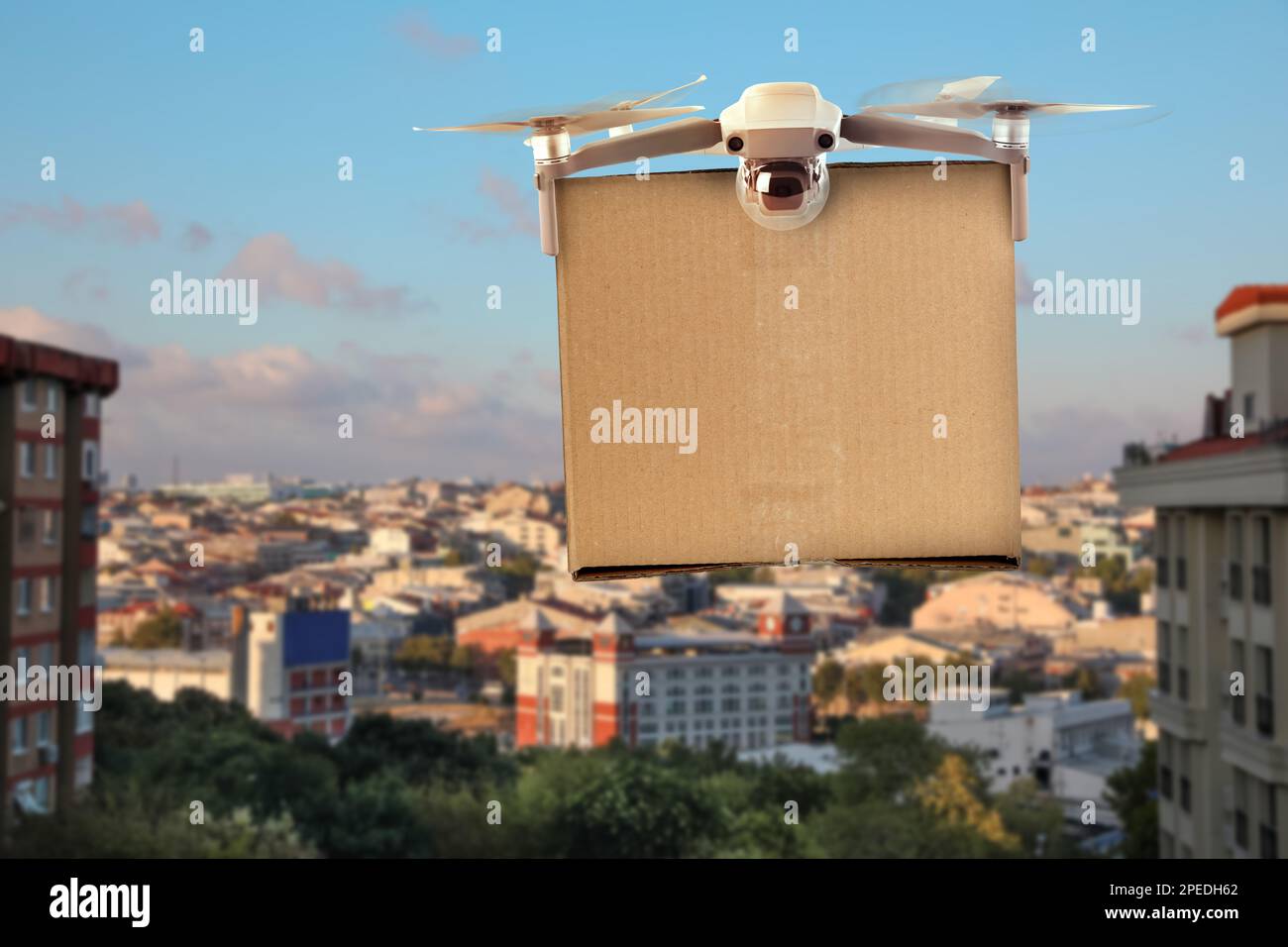Modern drone with carton box flying above city on sunny day. Delivery ...