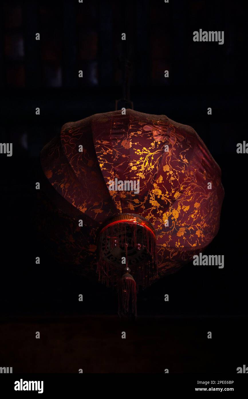 Red Asian fabric lantern hanging unlit from the ceiling in a dark room ...