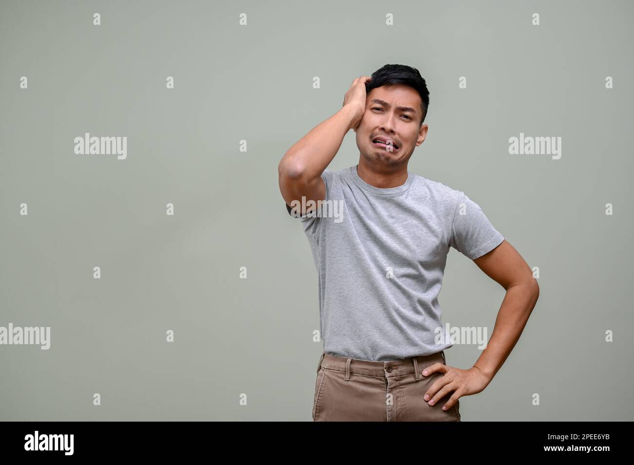 Crying and sad millennial Asian man in casual clothes stands against an ...