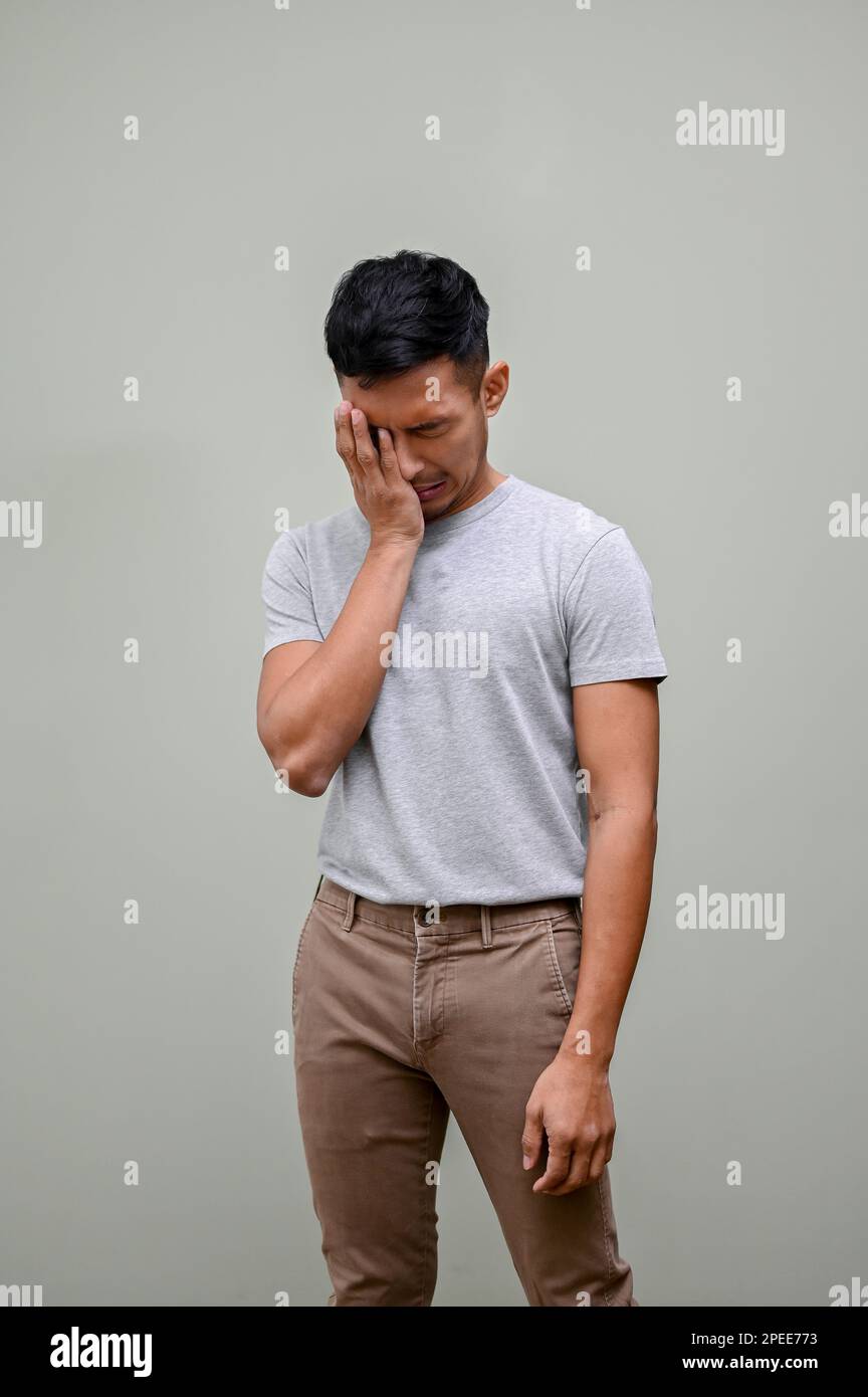Sad and crying millennial Asian man in casual clothes covering his face ...