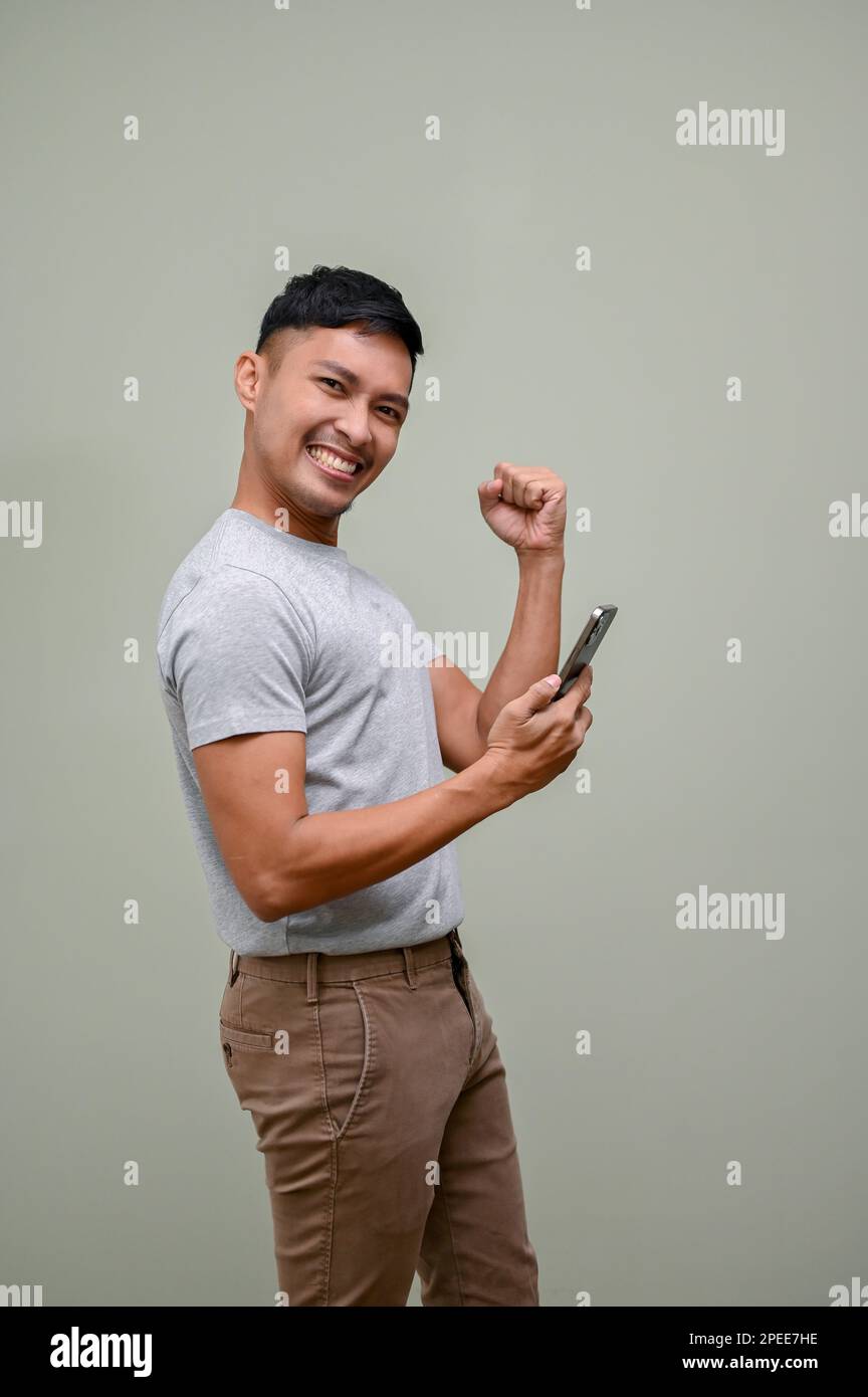Smiling and excited millennial Asian man in casual clothes holding his ...