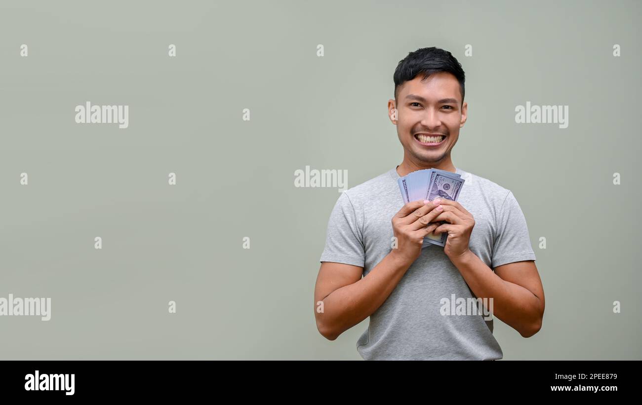 Smiling and happy millennial Asian man in casual clothes holding cash ...