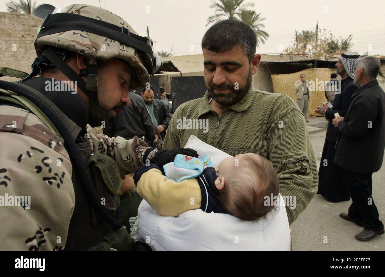 An Iraqi Army soldier checks a baby as it arrives with his father and ...