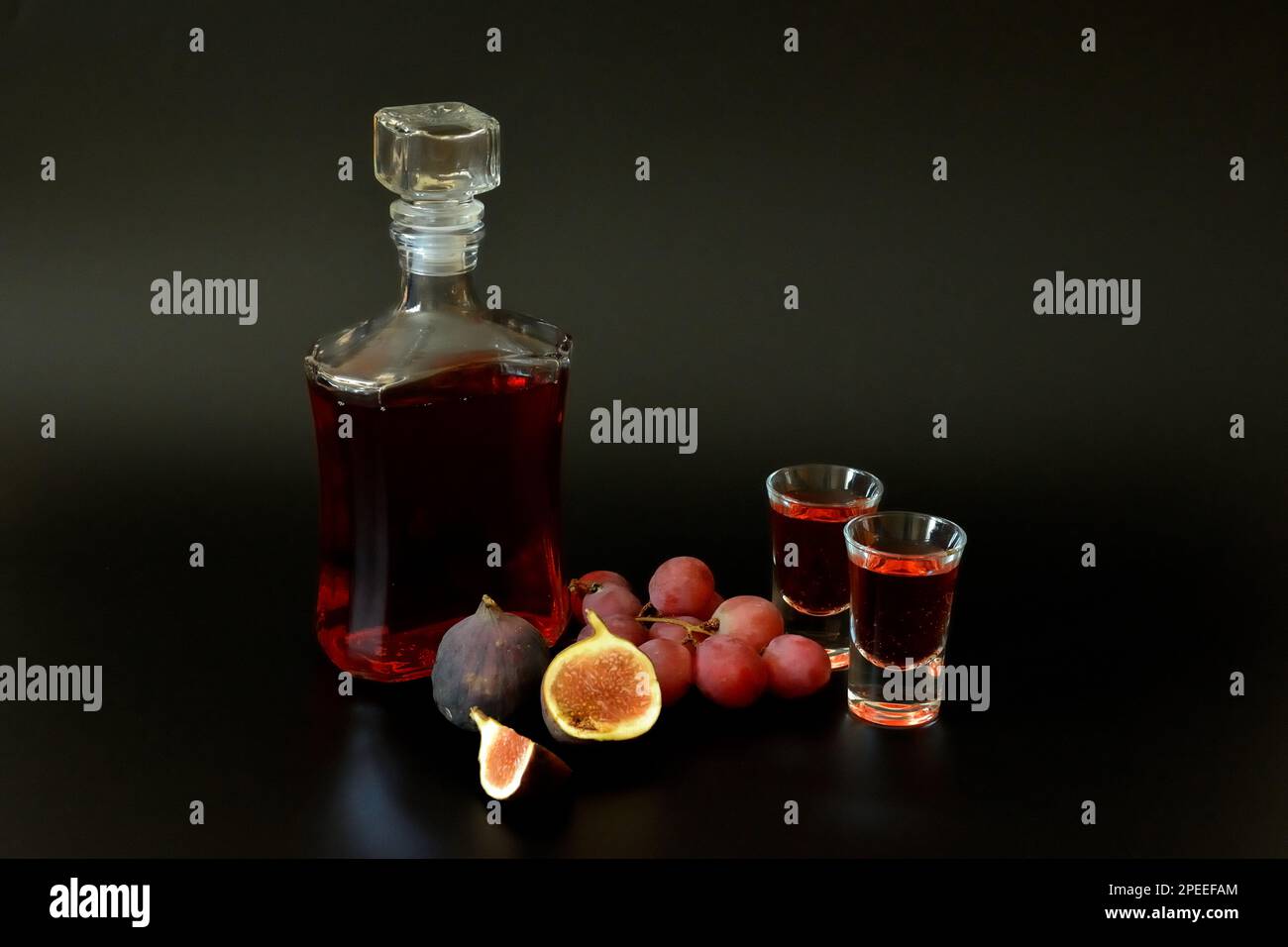 An antique glass decanter and two glasses of homemade liqueur on a black background, next to ...