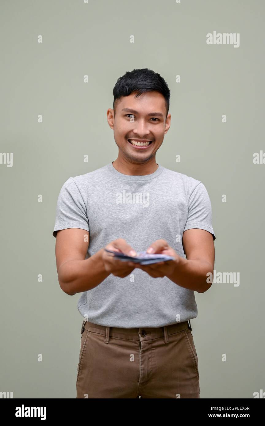 Happy and smiling millennial Asian man in causal clothes handing money ...