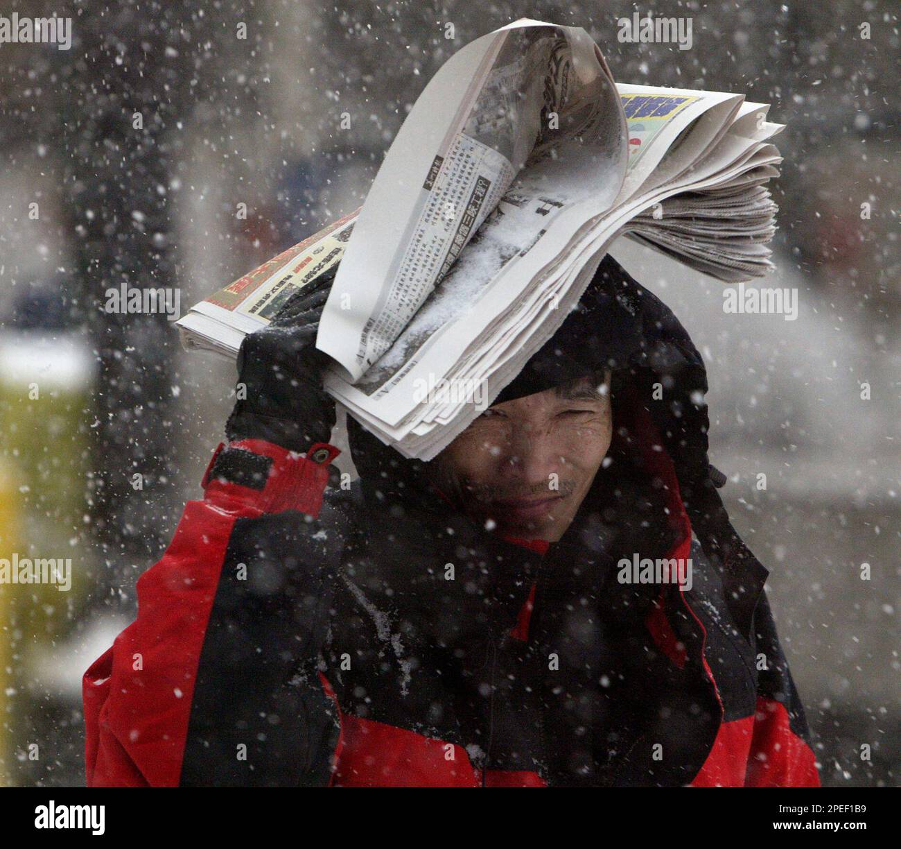 A man crosses the street shielding himself from blowing snow with a ...