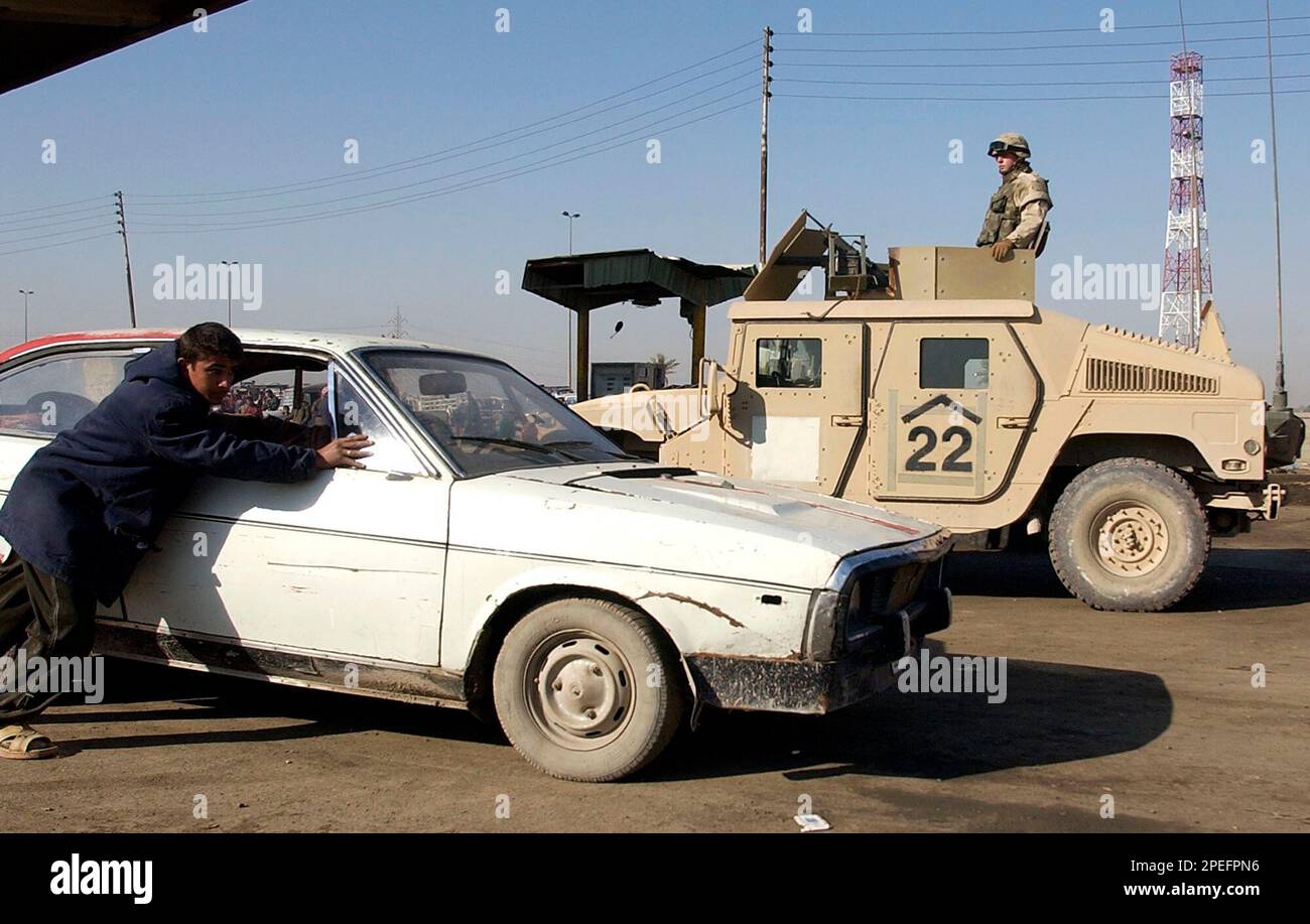 An Iraqi man pushes his car past an US Humvee at the petrol station to ...