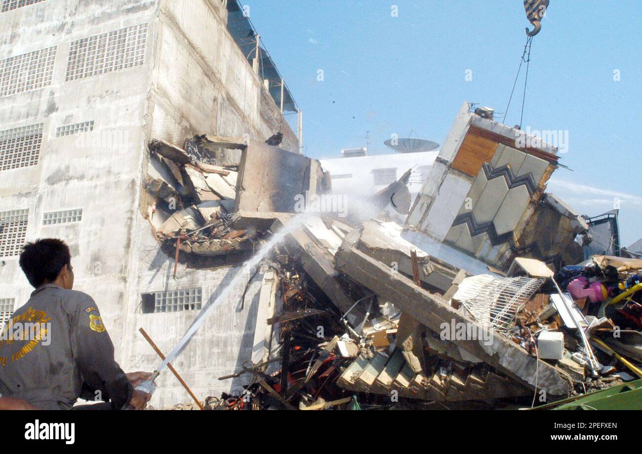 A Thai firefighter sprays water as a crane lifts debris after ...