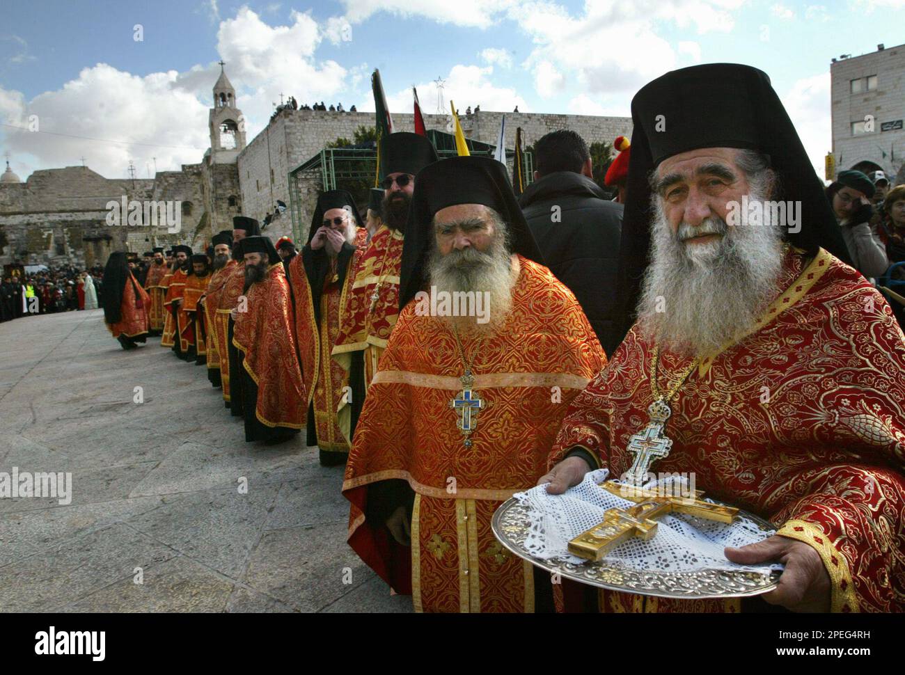 Greek Orthodox priests, one holding a golden cross, stand outside the ...