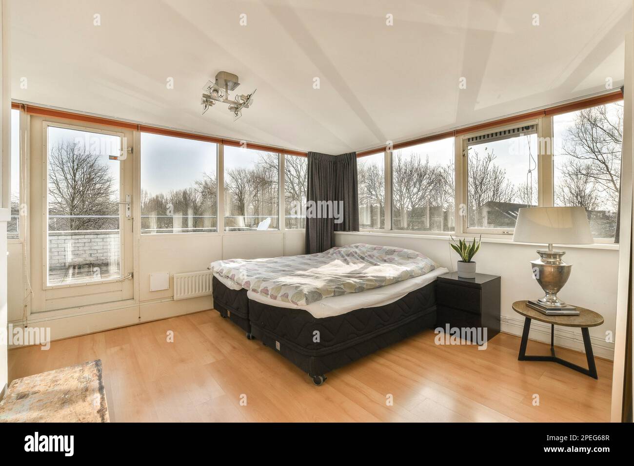 a bedroom with wood flooring and large windows looking out onto the ...