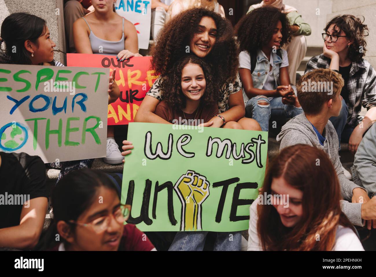 Happy teenage girls smiling at the camera while sitting with a crowd of ...