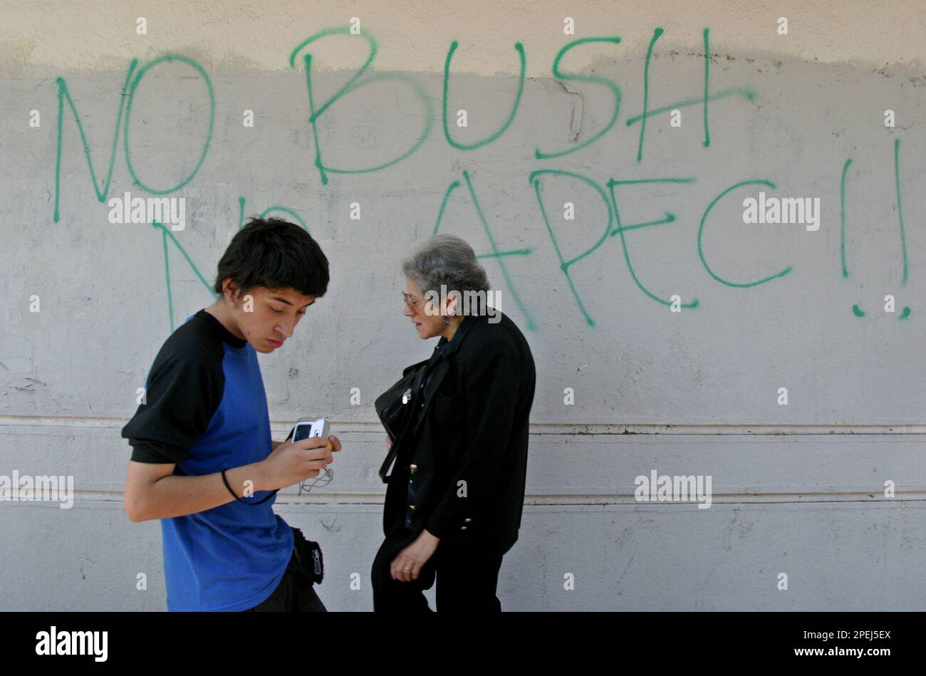 People walk past in front graffiti which reads "No Bush, No APEC ...