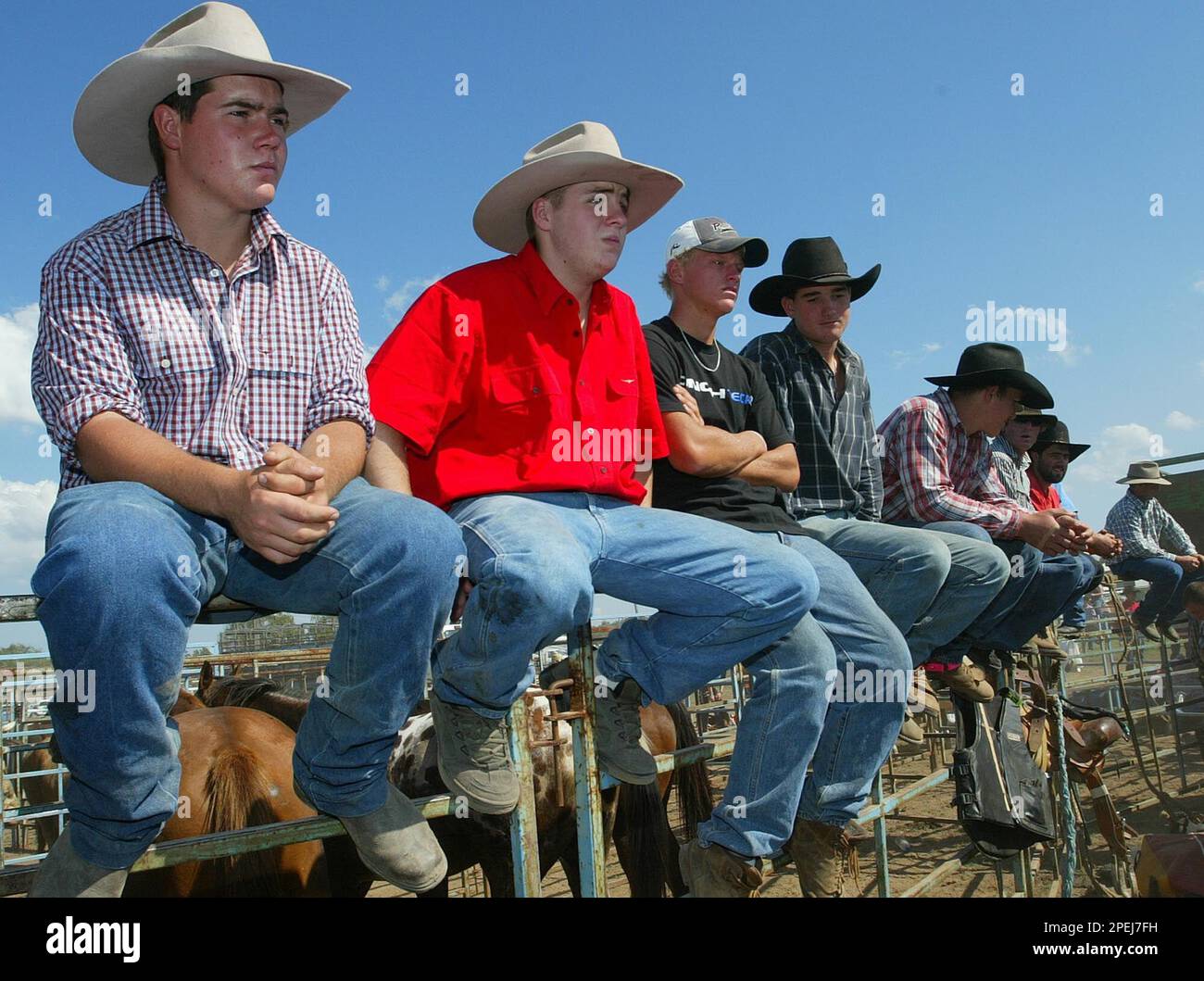 Young cowboys wearing broad-brimmed felt hats, sit on a fence at an ...