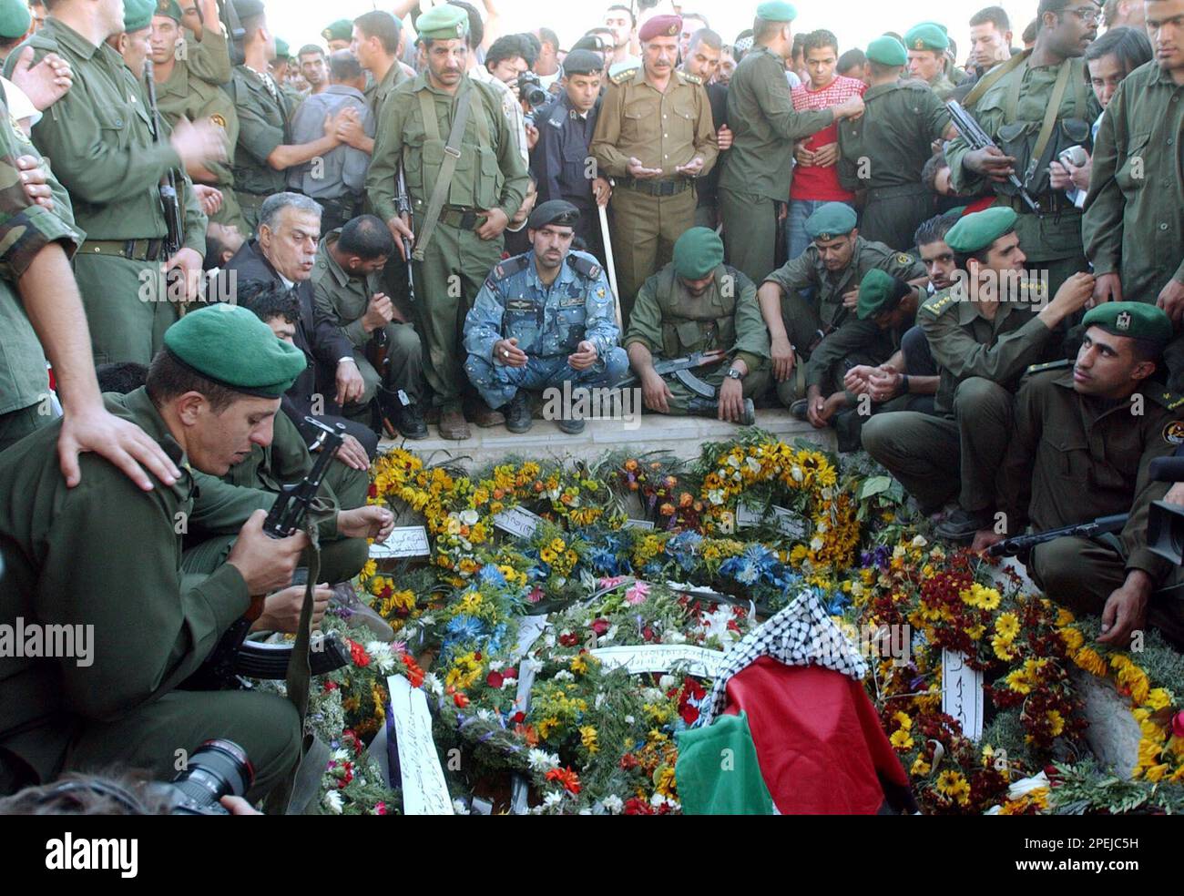 Palestinian security officers and mourners gather around the grave of ...