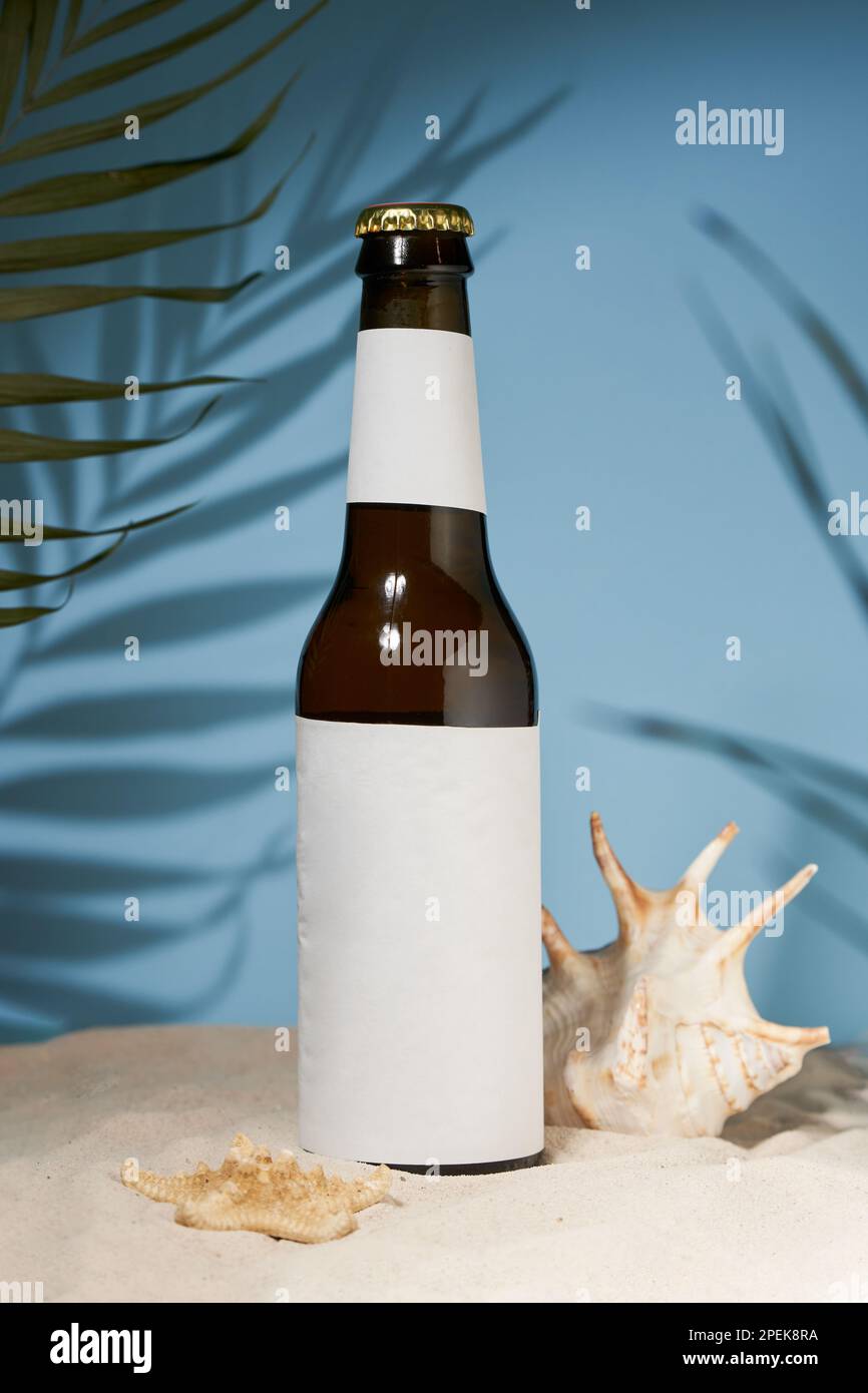 Capped bottle of beer or ale standing in the golden sand with shells ...