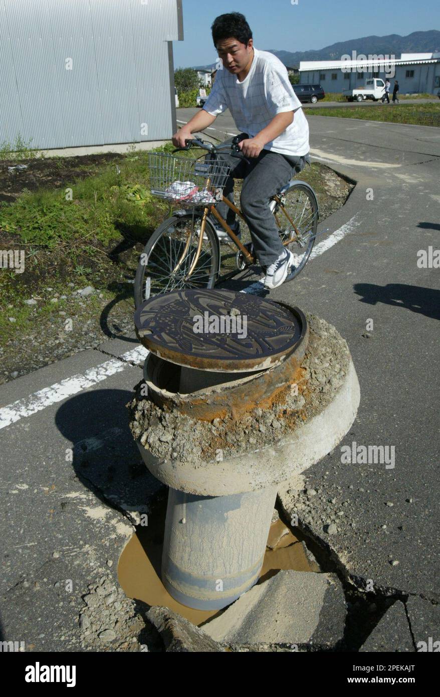 A man rides a bike past a manhole protruded from a road in Ojiya ...