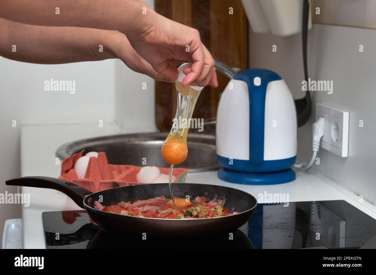Cooking scrambled eggs with ham. Breaking an egg Stock Photo - Alamy