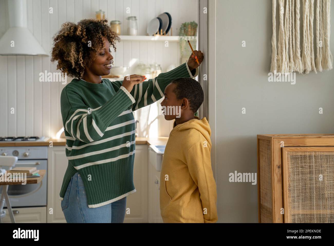 African American stay-at-home mom measuring height of kid son at home ...