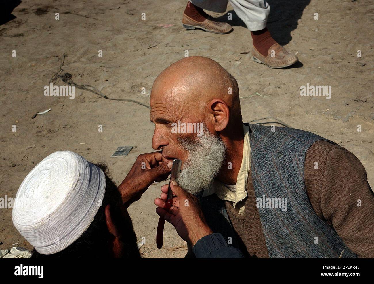 An elderly Afghan has his beard trimmed by a street barber on the first ...