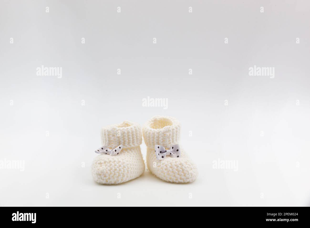 Knitted white baby booties with polka-dot bows on a gray isolated ...