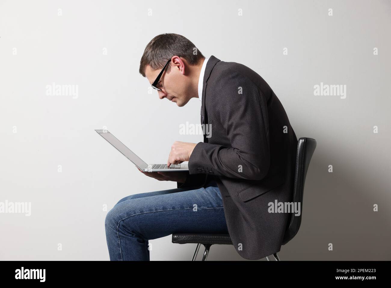 Man with bad posture using laptop while sitting on chair against grey ...