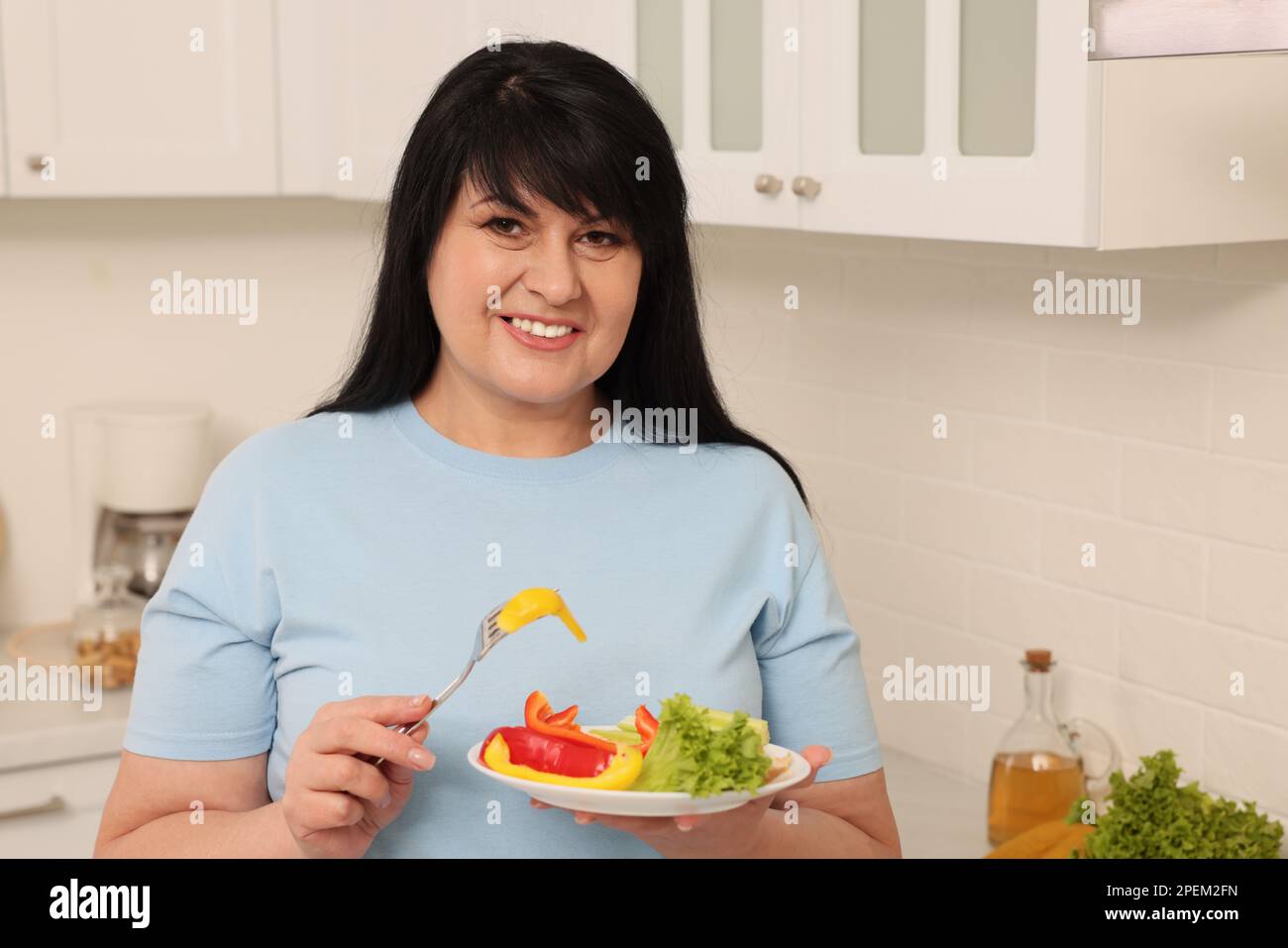 Happy overweight woman eating salad in kitchen. Healthy diet Stock ...
