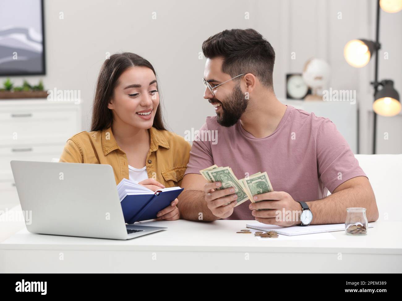 Happy young couple counting money at white table indoors Stock Photo ...