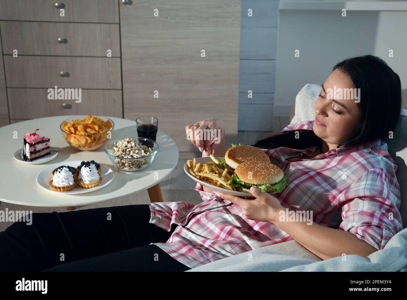 Happy Overweight Woman Eating French Fries With Burgers At Home Stock