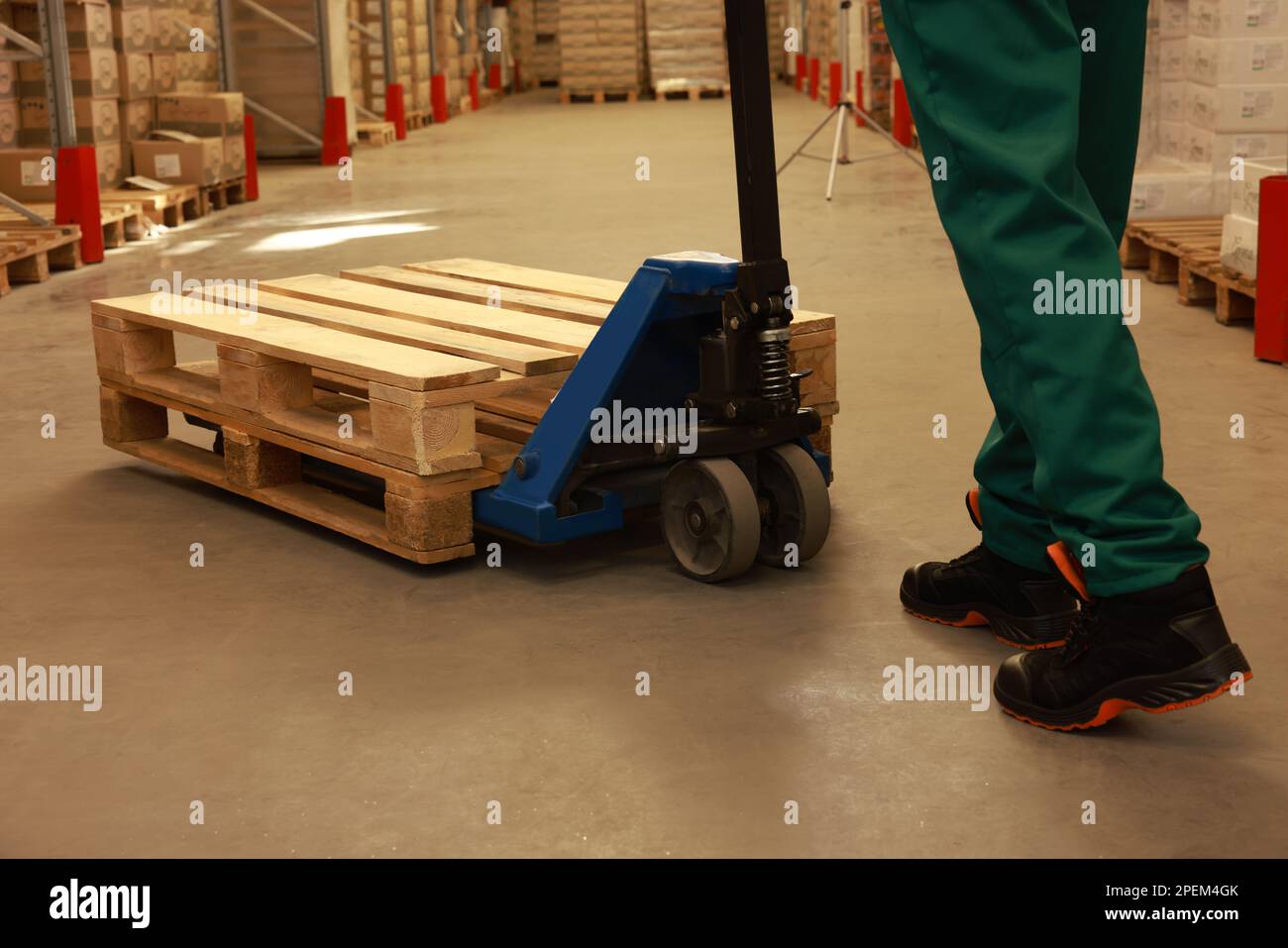 Worker moving wooden pallets with manual forklift in warehouse, closeup ...