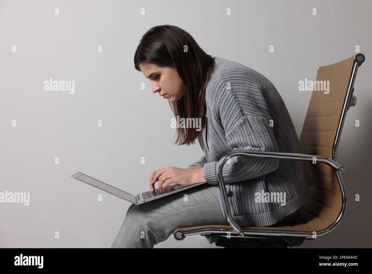 Young woman with bad posture using laptop while sitting on chair ...