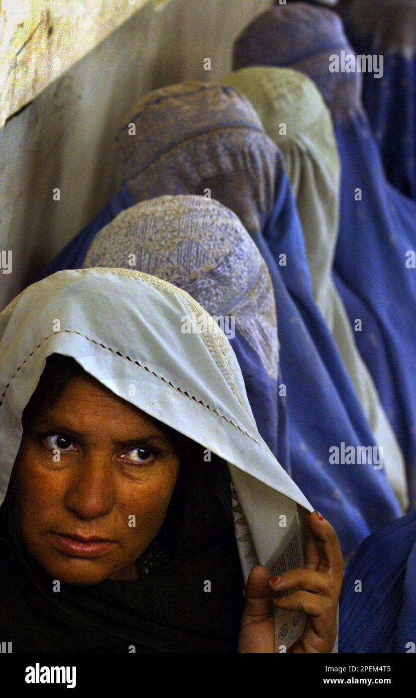 An Afghan woman lifts her traditional blue burqa awaits in a line ...