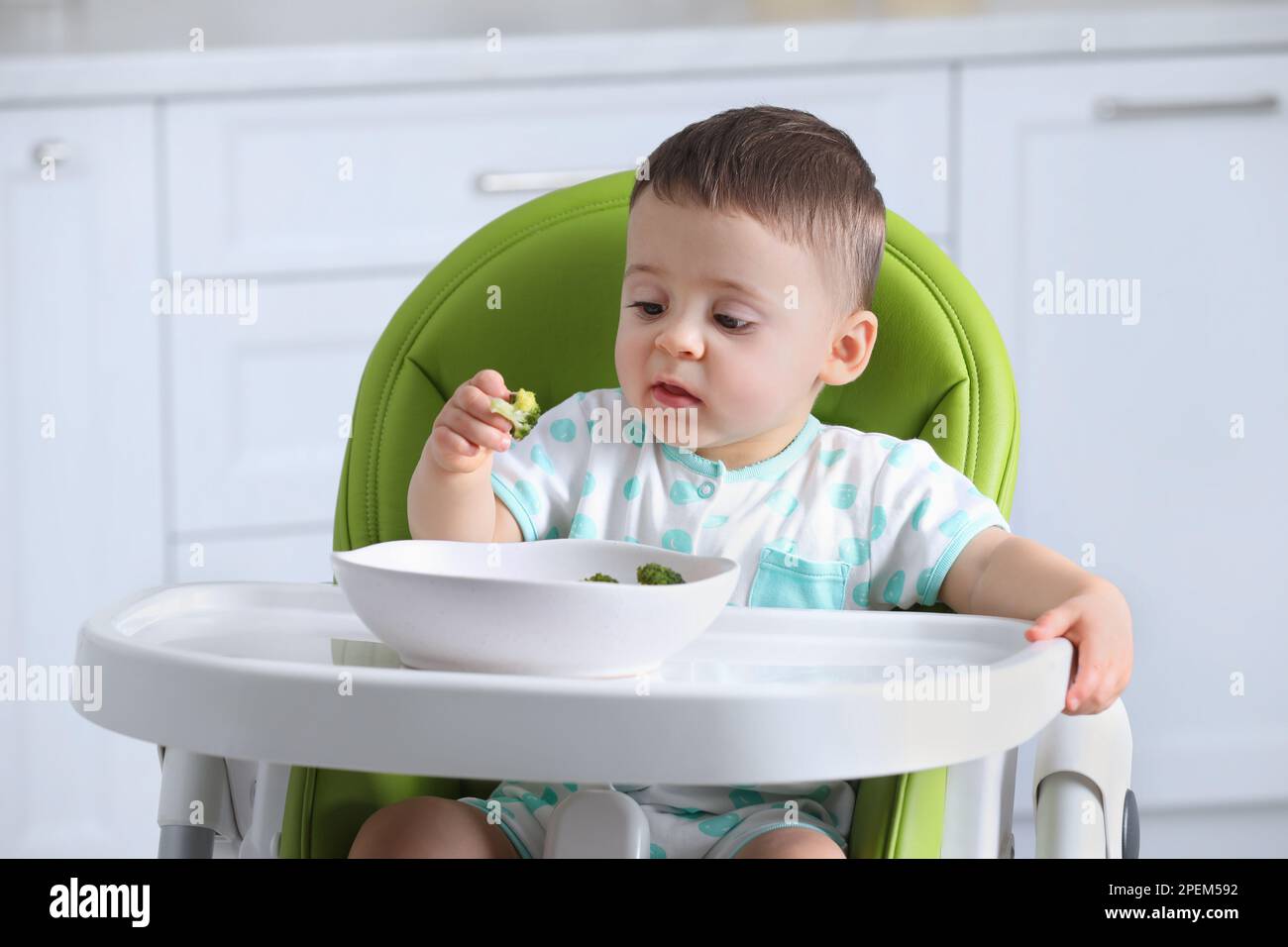 Cute little baby eating healthy food in high chair at home Stock Photo ...