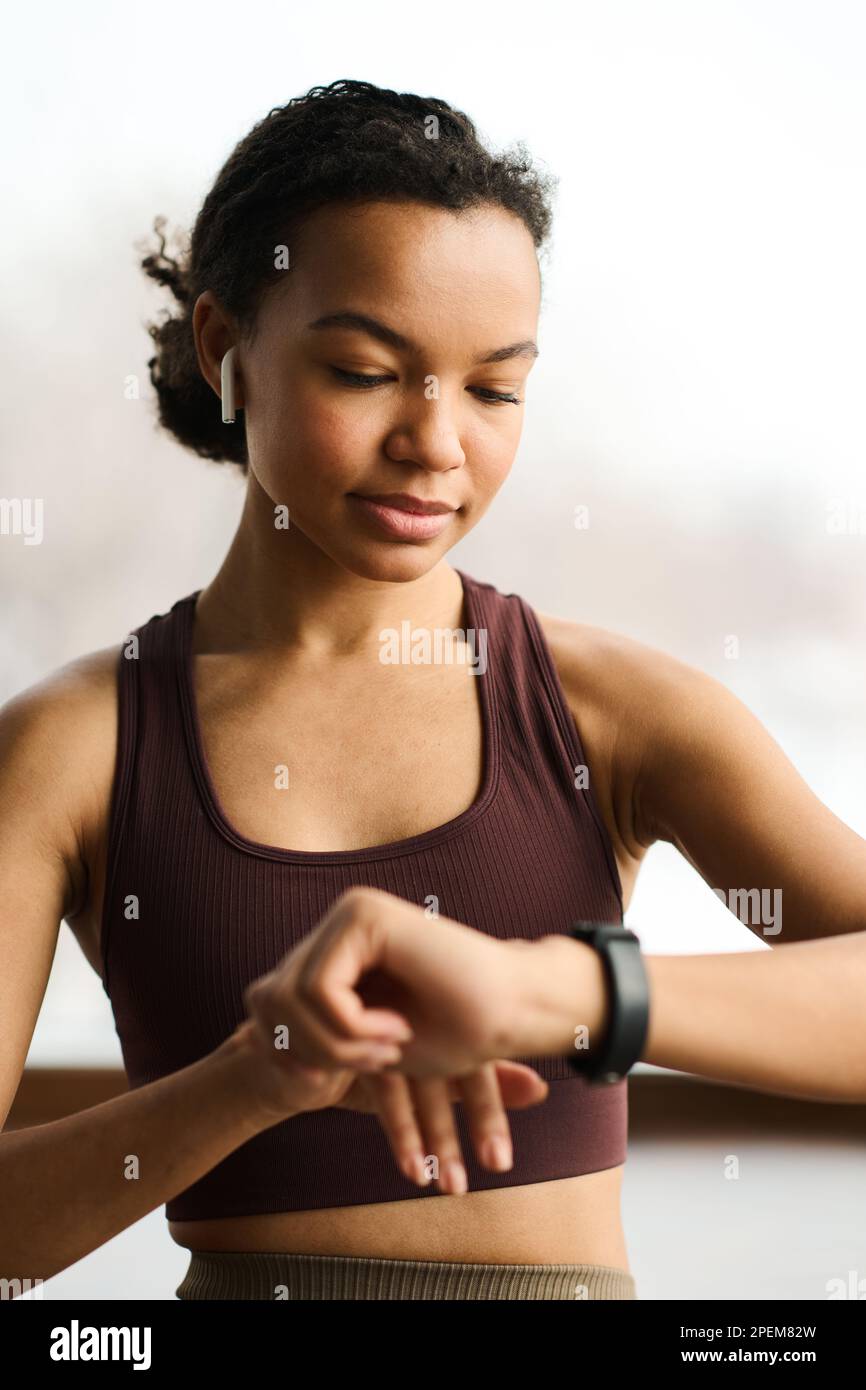 Vertical image of young girl checking her fitness bracelet after sport ...