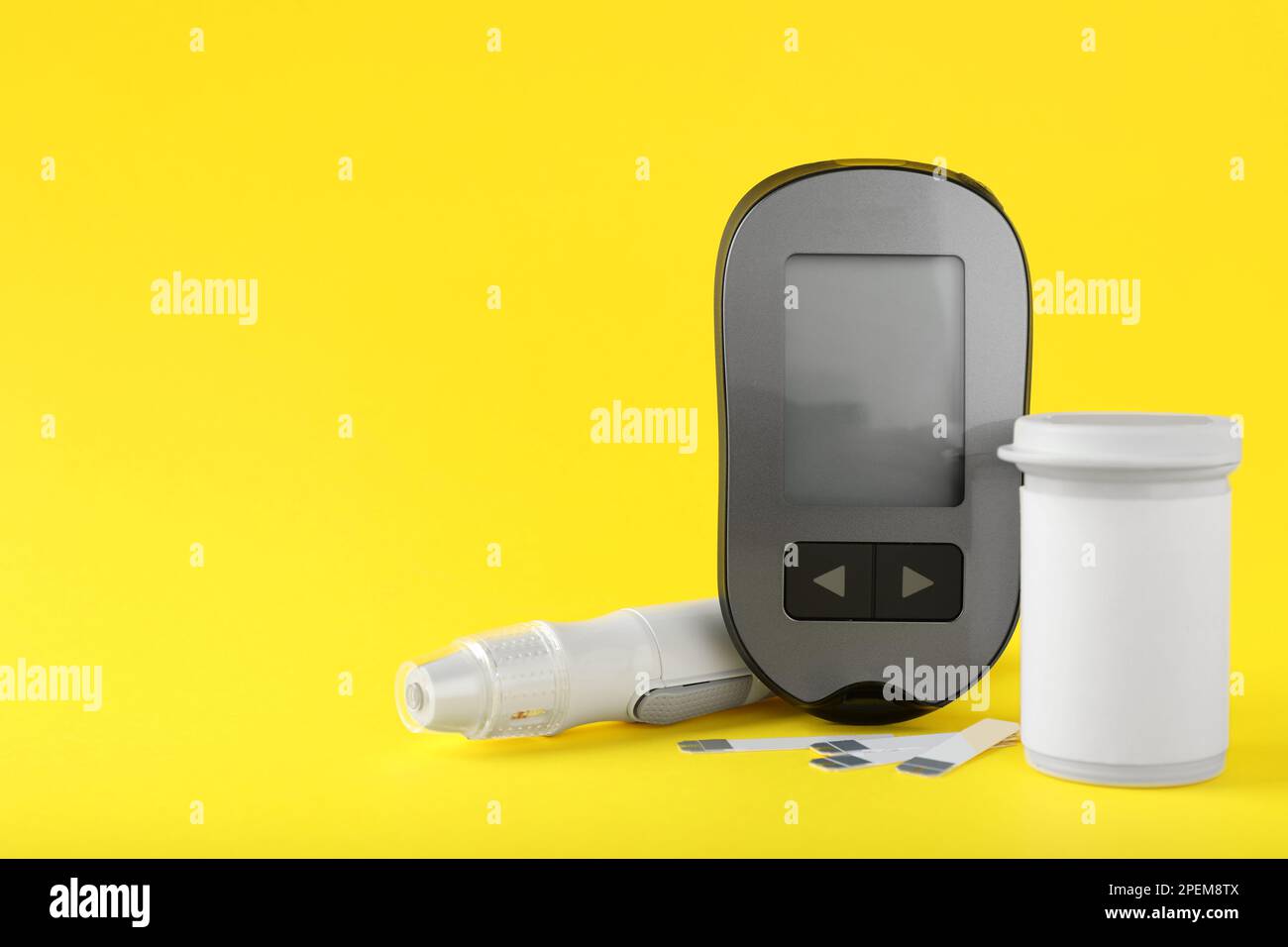 Digital glucometer, lancet pen, container and test strips on yellow ...
