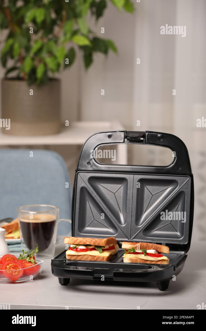 Modern grill maker with sandwiches and coffee on light grey table ...