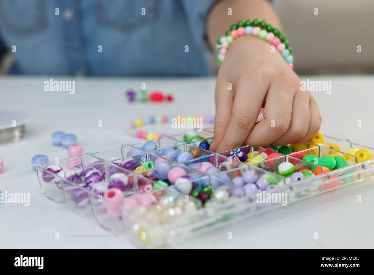 Little girl making beaded jewelry at table, closeup Stock Photo - Alamy