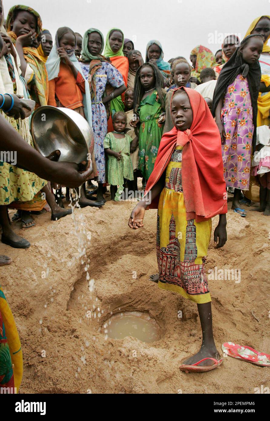 A girl hands out water from a hole dug in the sand of a wadi (dry ...