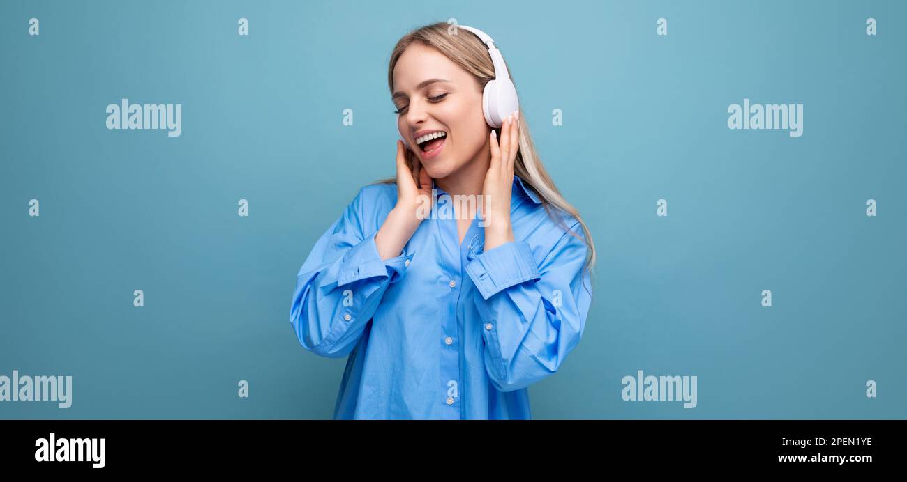 shy blonde girl in a casual shirt listens to songs in big headphones ...