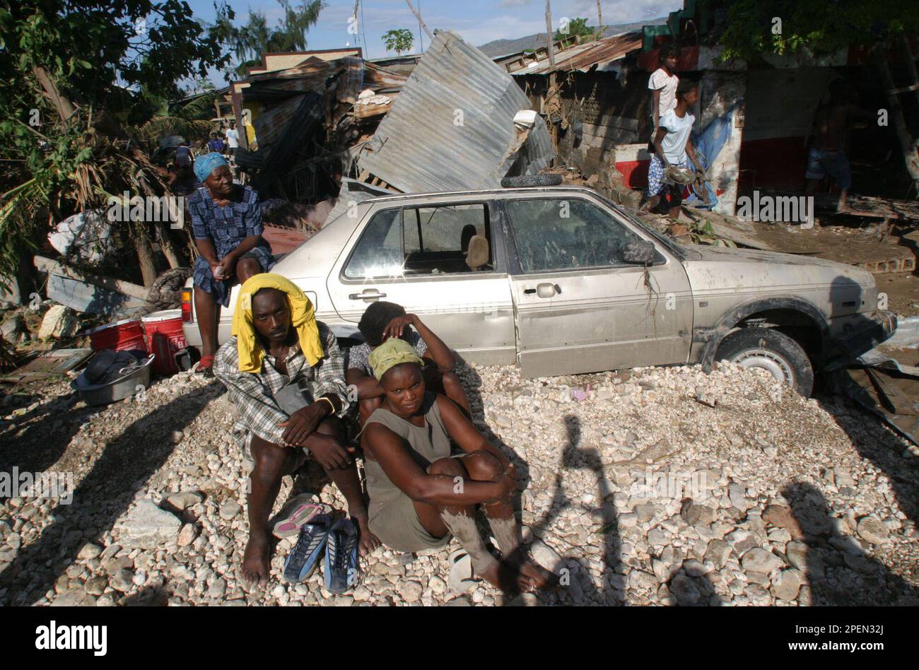 People sit in rubble next to cars destroyed and debris in Gonaives ...