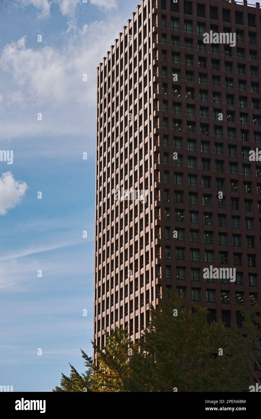 A high rise brown building stands amongst tall trees and lush green ...