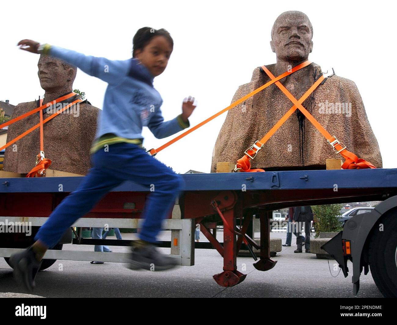 A child runs past a Lenin statue made of stone, right, and another ...