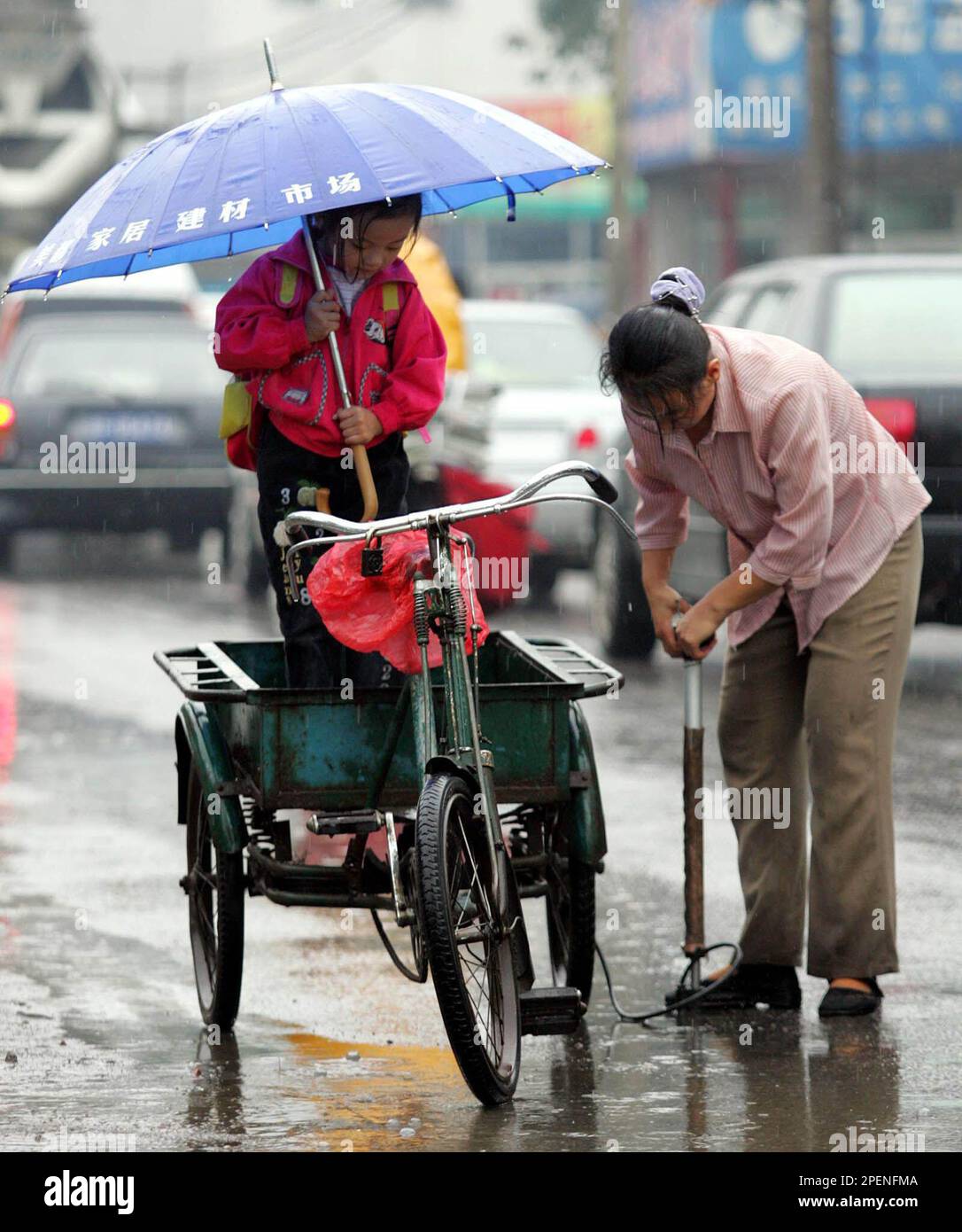 A young girl shelters under an umbrella as her mother pumps up the ...