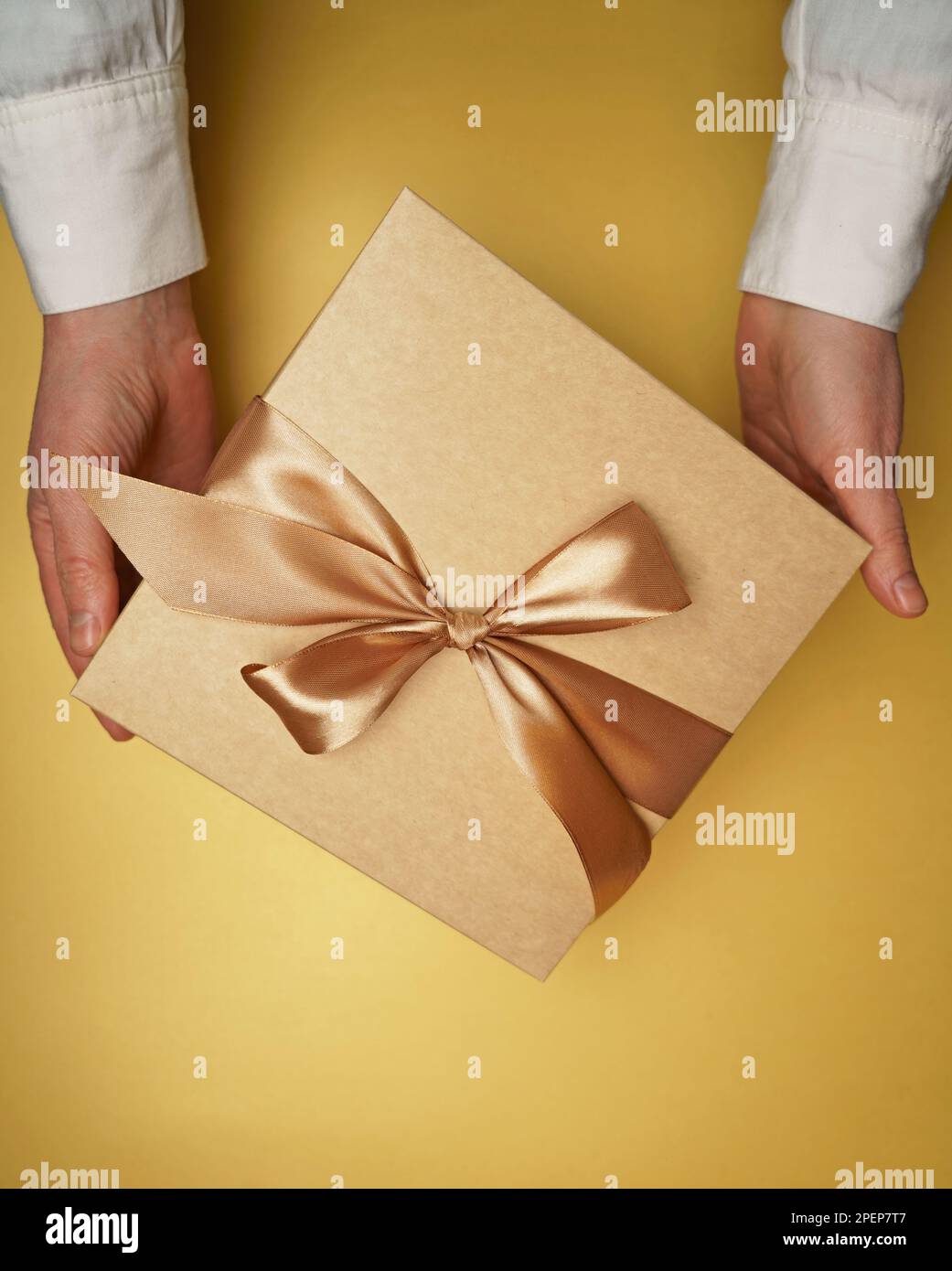On a yellow flat background hands hold a gift Stock Photo - Alamy