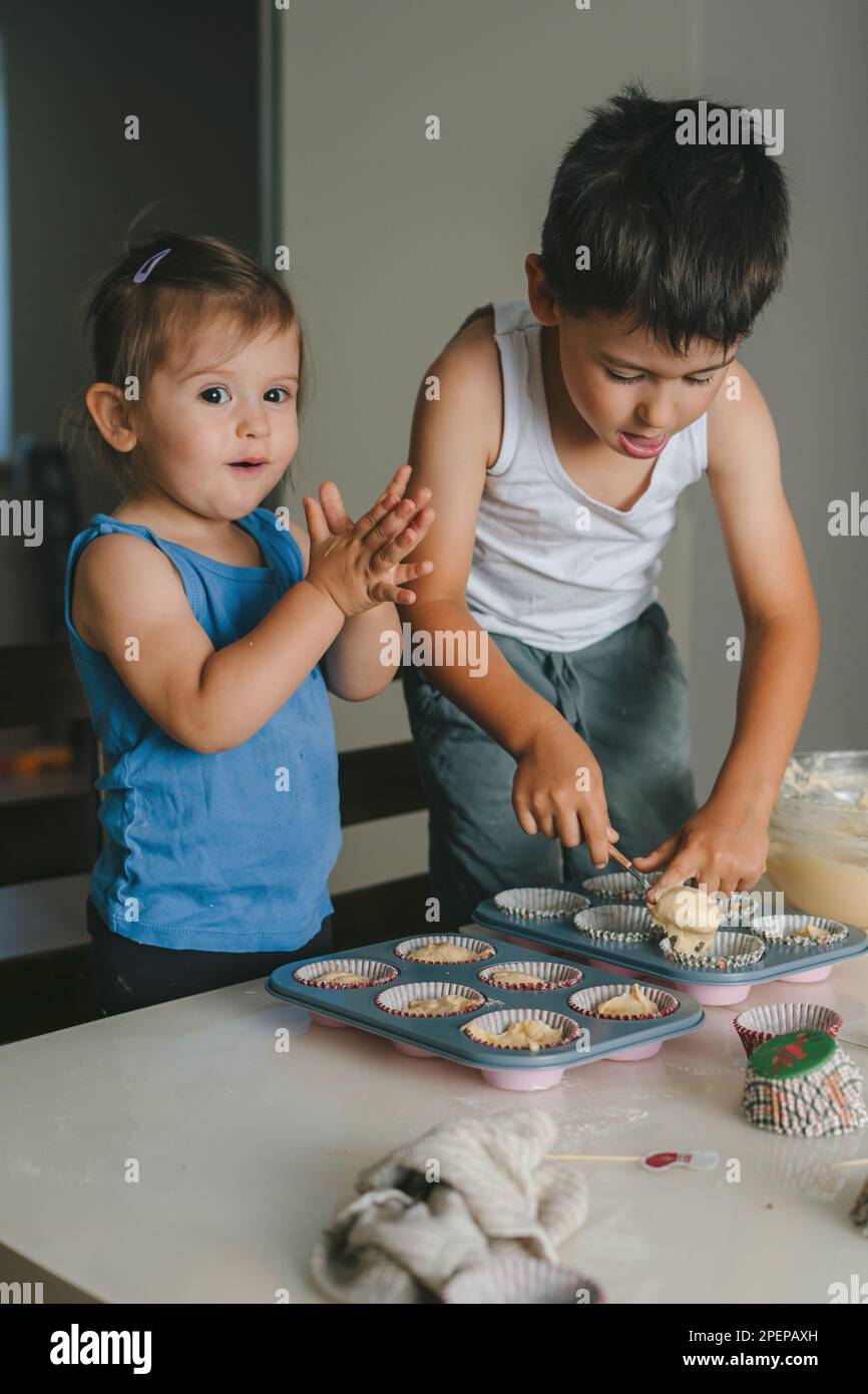Little baby girl and boy learning to make cup cakes, pouring cake ...