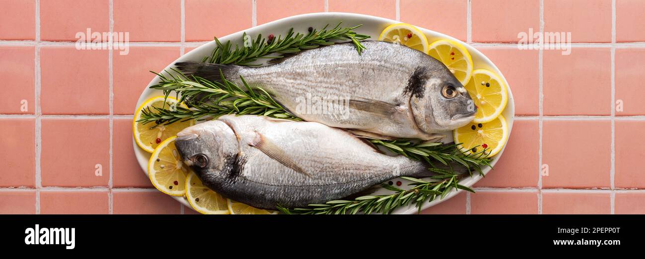 Dorada fish with lemon slices and rosemary sprigs in an oval dish on a ...