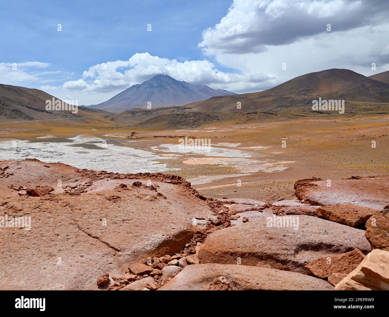 A desert with salt flats surrounded by large volcanoes dominating the ...