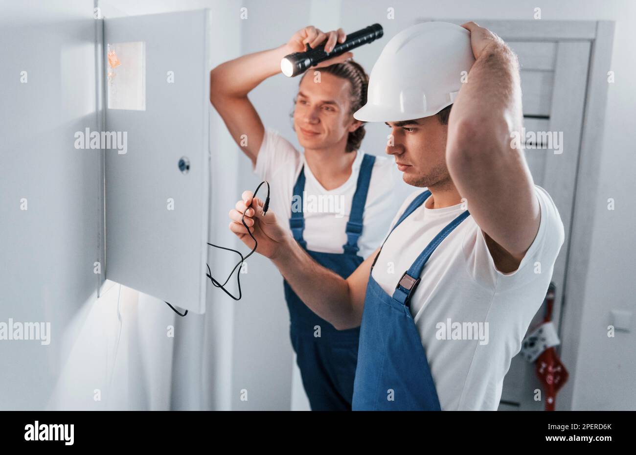 Two young male electricians works indoors together. Using flashlight ...