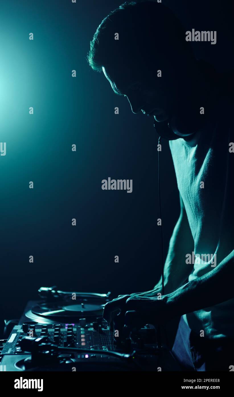 DJ playing techno music in dark nightclub. Silhoutte of cool young disc ...